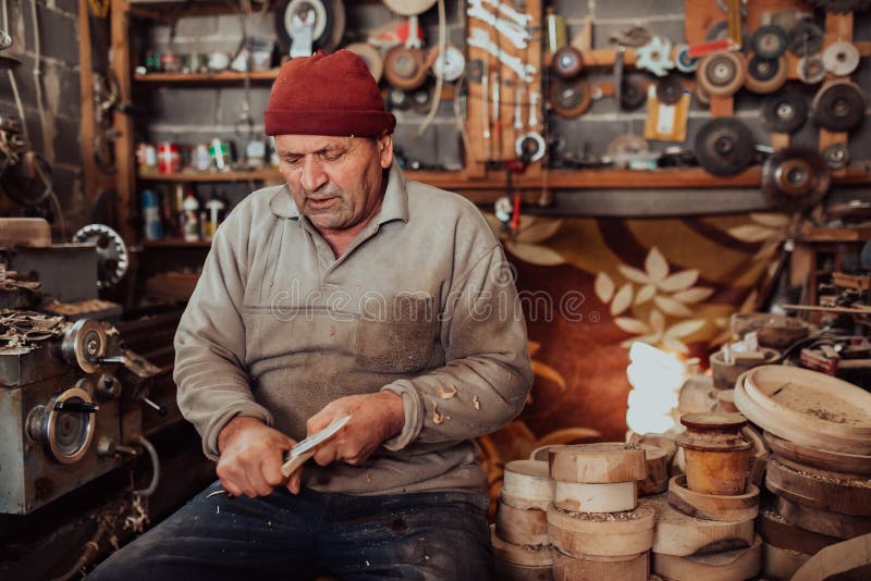 A Senior Man Sitting in the Workshop and Processing Wooden Utensils in ...