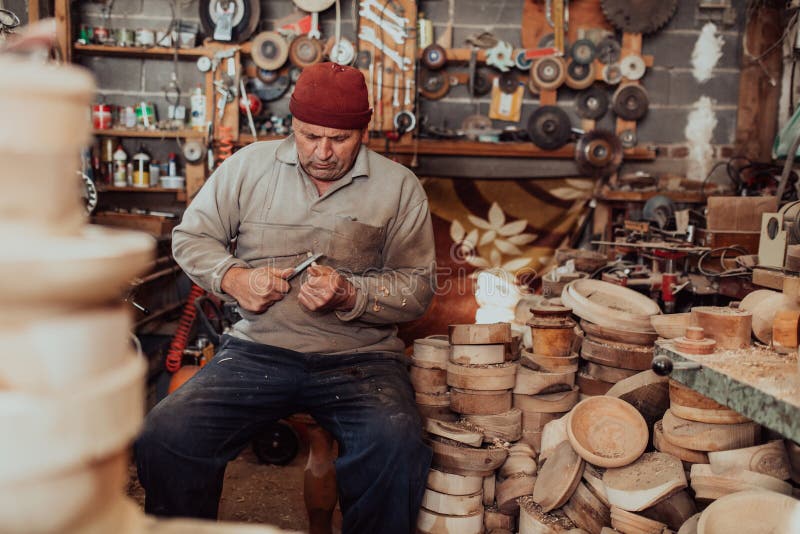 A Senior Man Sitting in the Workshop and Processing Wooden Utensils in ...