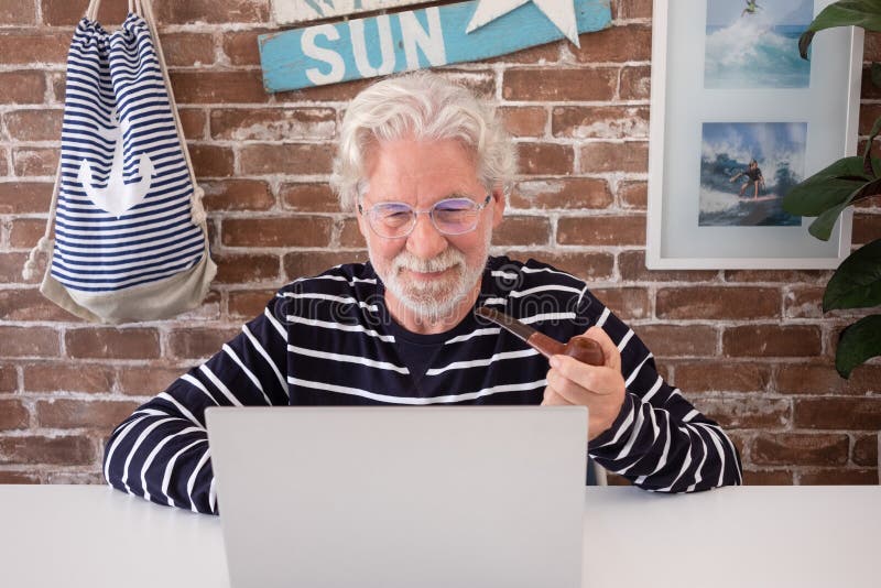 Senior Man Smoking Pipe while Using Laptop Computer at Home. Brick Wall ...