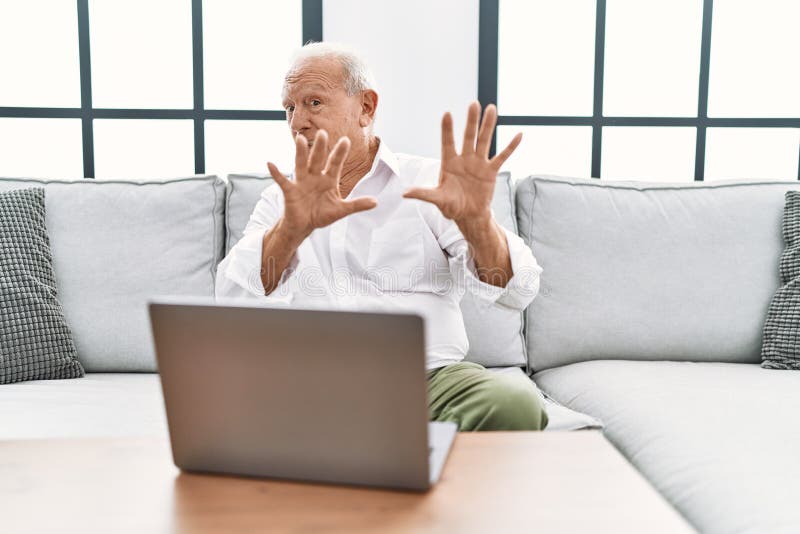 Senior Man Using Laptop at Home Sitting on the Sofa Afraid and ...