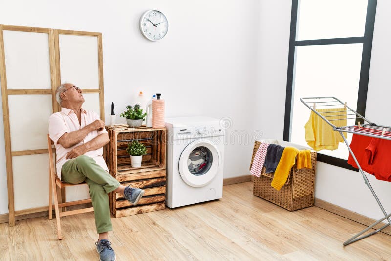 Senior Man Waiting For Washing Machine Sitting On Chair At Laundry Room