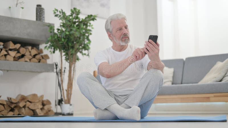 Old Man Using Smartphone on Excercise Mat at Home Stock Photo - Image ...
