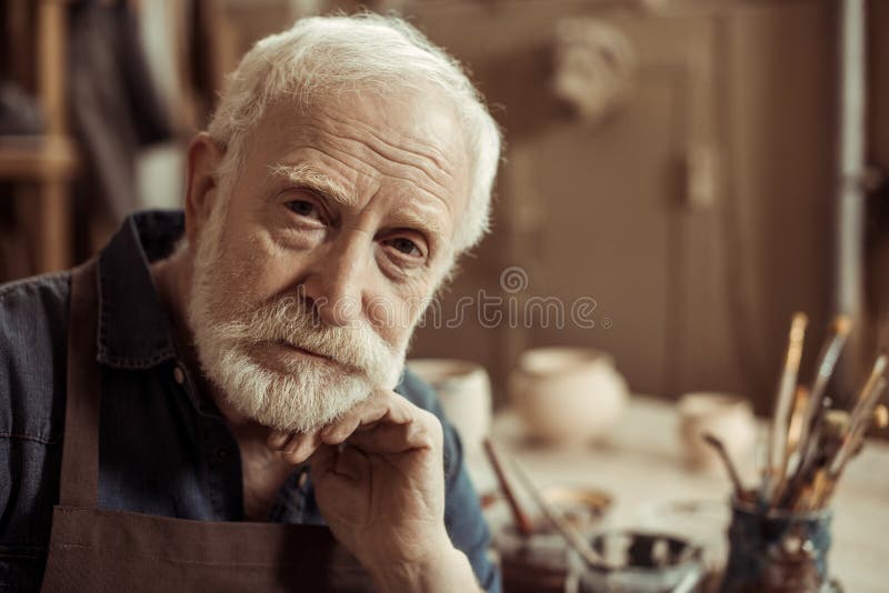 Senior Potter in Apron Sitting at Table and Looking at Camera Stock ...