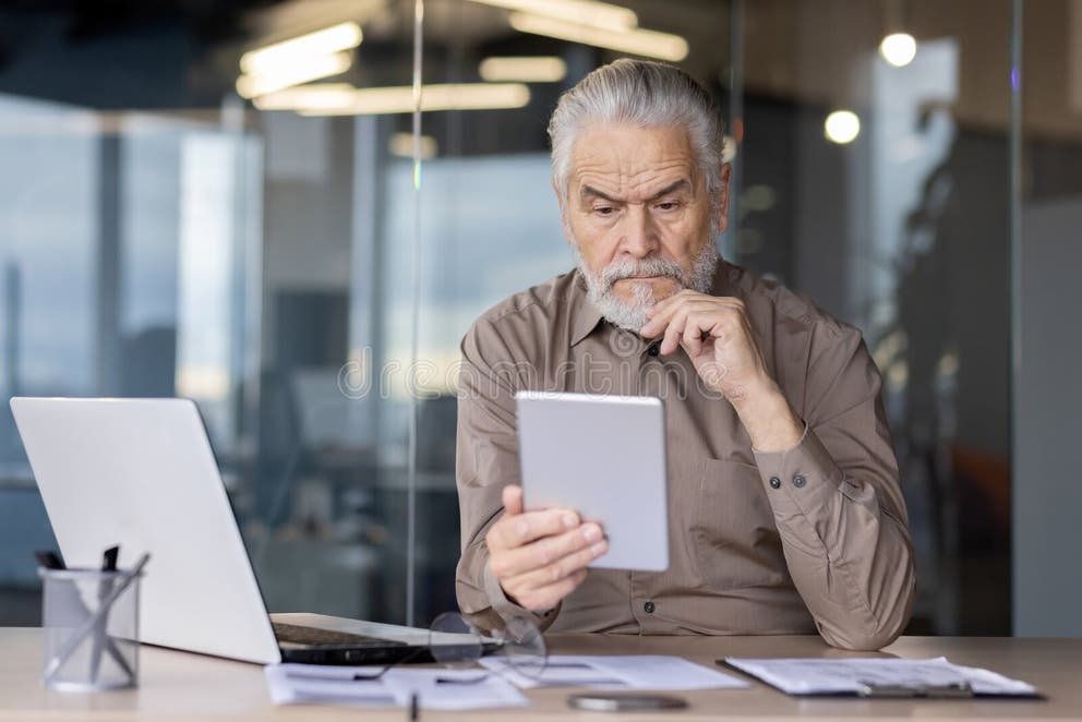 A Senior Professional Man is Examining Data on a Tablet in an Office ...
