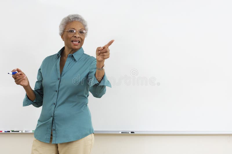 Senior Teacher Pointing while Gesturing Against White Board in ...