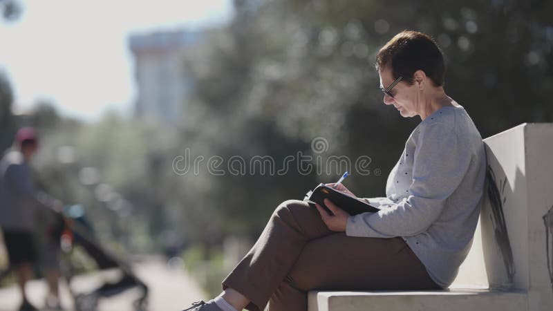 Woman Writing Notes in Notebook Sitting on Bench in Park Stock Video ...