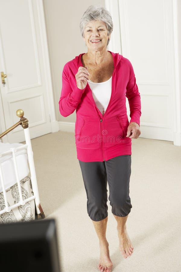 Senior Woman Exercising Whilst Watching Fitness Dvd On Television Stock