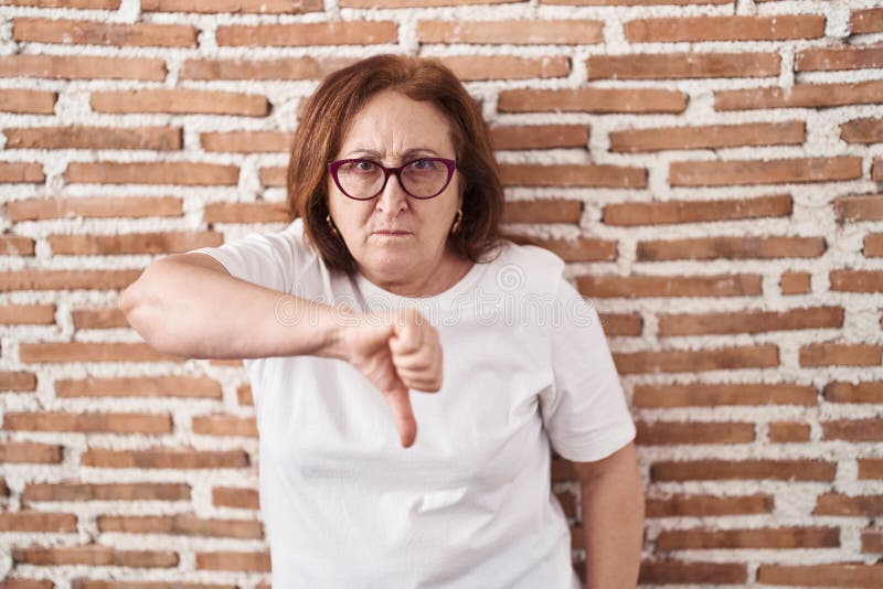 Senior Woman With Glasses Standing Over Bricks Wall Looking Unhappy And