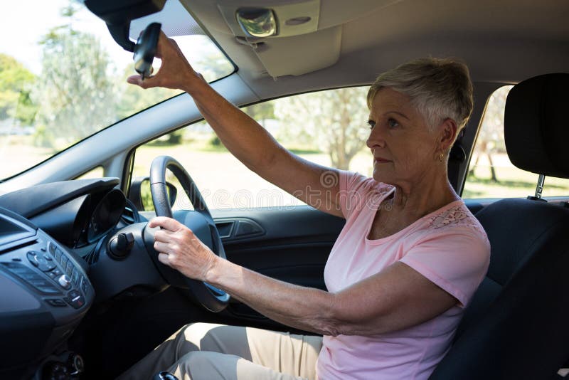 Senior Woman Looking into Rear View Mirror while Driving a Car Stock ...