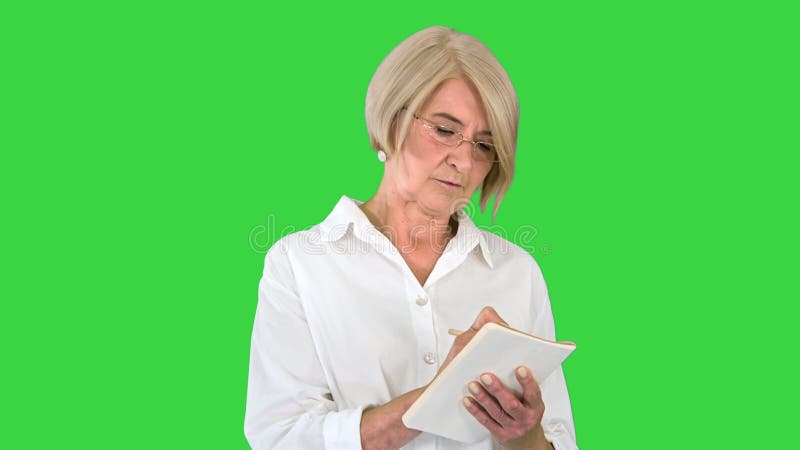Senior Woman Making Notes in Notepad on a Green Screen, Chroma Key ...