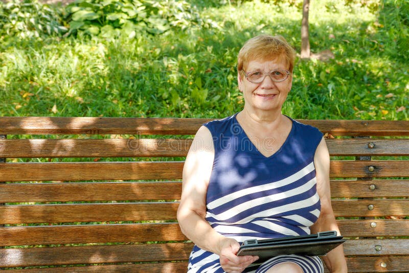 Senior Woman in the Park on a Bench with a Tablet on a Sunny Day Stock ...