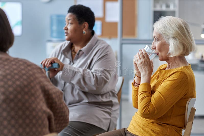 Senior Woman Sitting In Circle At Mental Health Support Group Stock