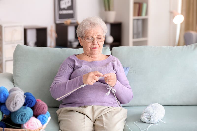 Senior Woman Sitting On Sofa While Knitting Sweater At Home Stock Image