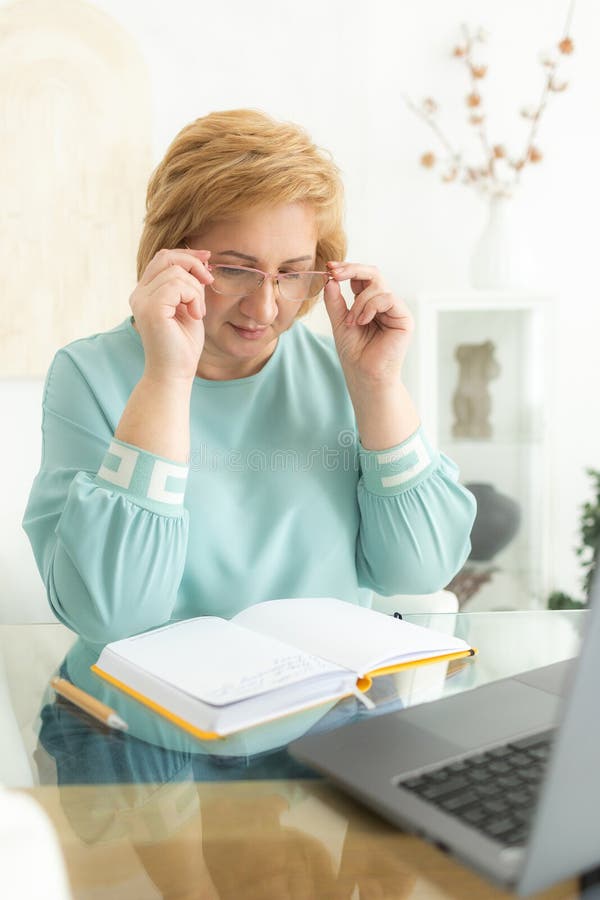 Senior Woman with Laptop and Notebook while Sitting at Table and ...