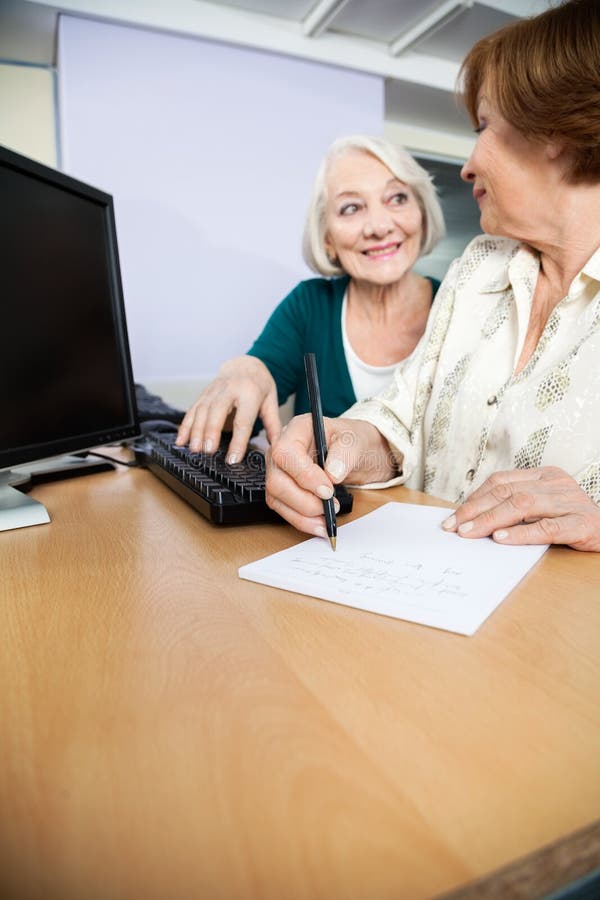 Senior Woman Using Computer while Classmate Writing Notes Stock Image ...