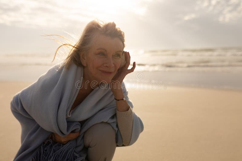 Senior Woman Wrapped in a Shawl Holding Sea Shell at Beach Stock Photo ...