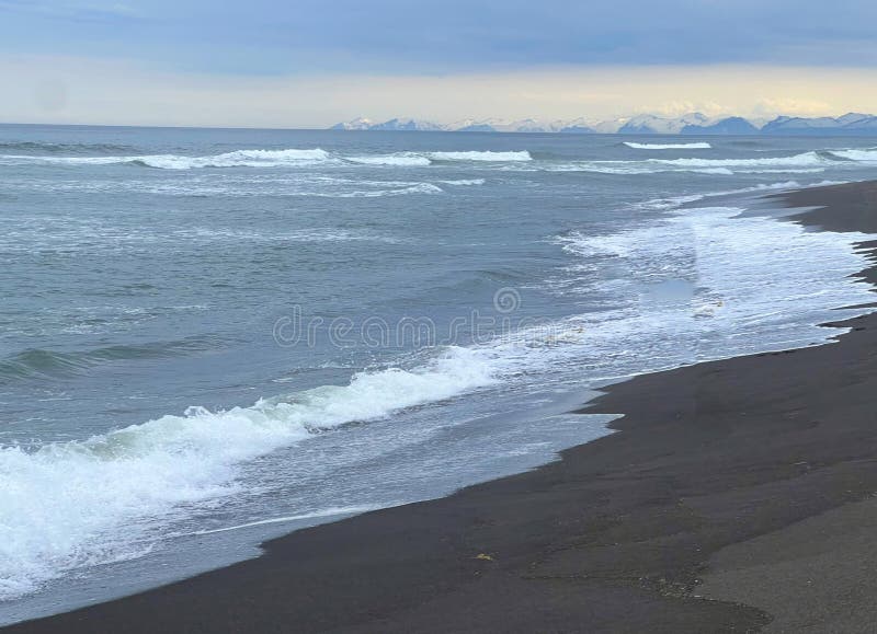 Serene Ocean Waves Lapping Dark Sandy Shore Under Cloudy Sky with ...