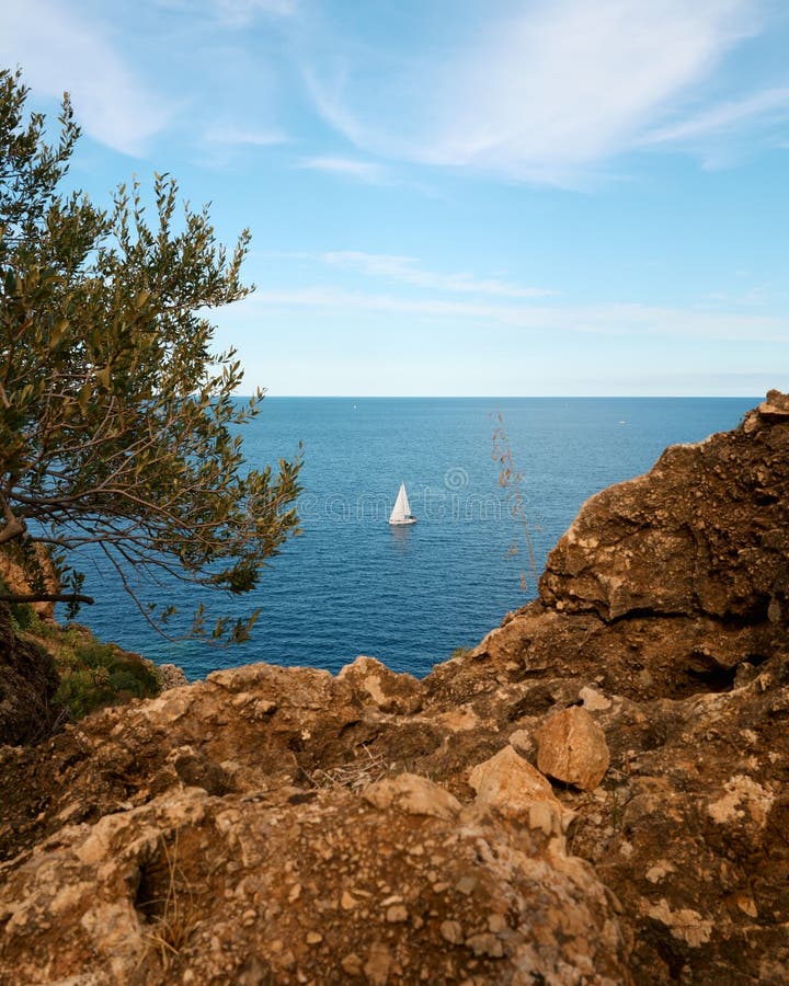 Serene View of a Sailboat on a Calm Sea Framed by Rocky Cliffs and ...