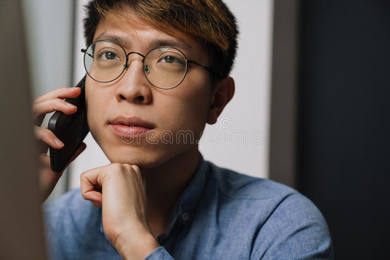 Serious Asian Guy Talking on Cellphone while Working with Laptop Stock ...