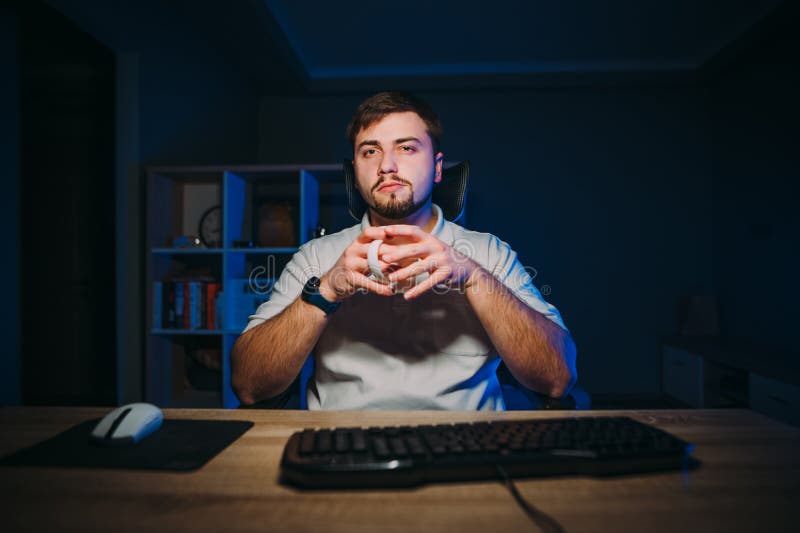 Serious Bearded Man with a Cup of Tea in His Hand Sits at the Computer ...