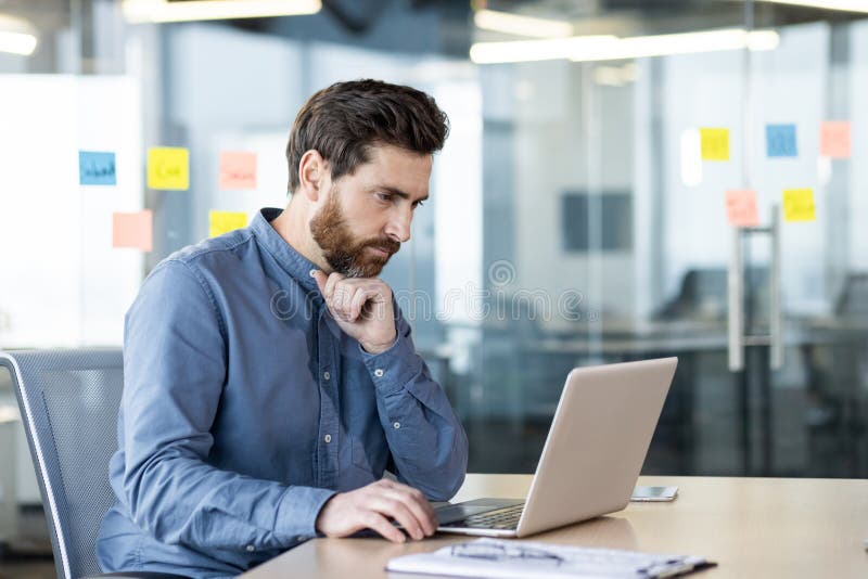 A Serious and Focused Young Man is Sitting at a Desk in the Office and ...