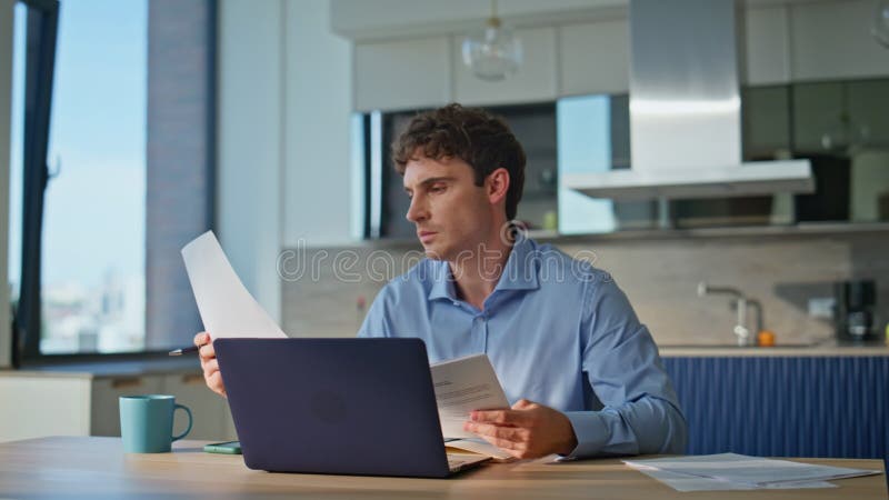 Serious Man Reviewing Documents Working on Laptop in Modern Home Office ...