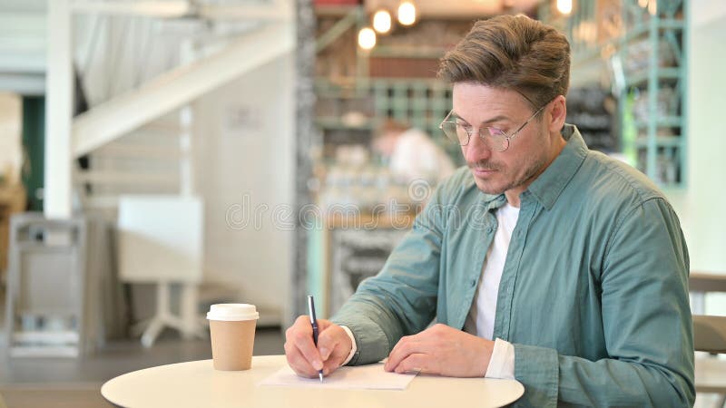 Serious Middle Aged Man Writing on Paper in Cafe Stock Photo - Image of ...