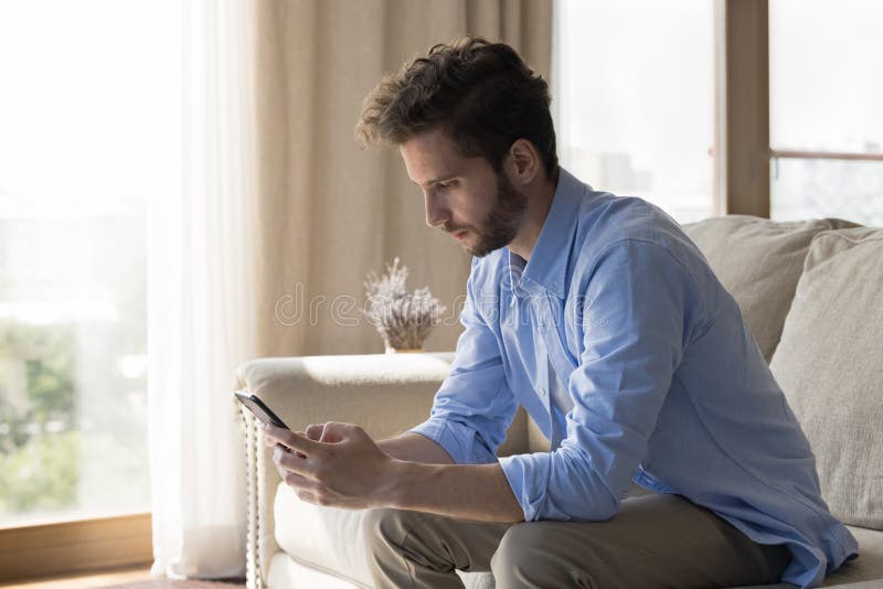 Serious Millennial Man Using Cellphone Seated on Sofa at Home Stock ... Serious Millennial Man Using Cellphone Seated on Sofa at Home Stock ...
