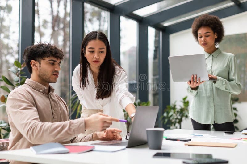Serious Multiethnic Coworkers Pointing at Laptop Solving Problems at ...