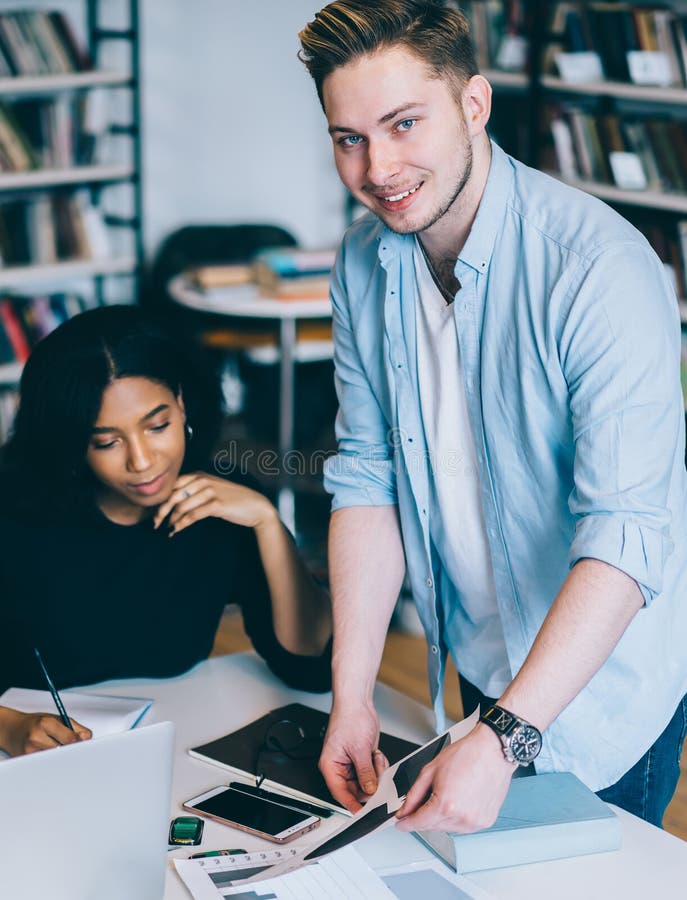 Serious Multiracial Women Writing at Table while Smart Man Standing and ...
