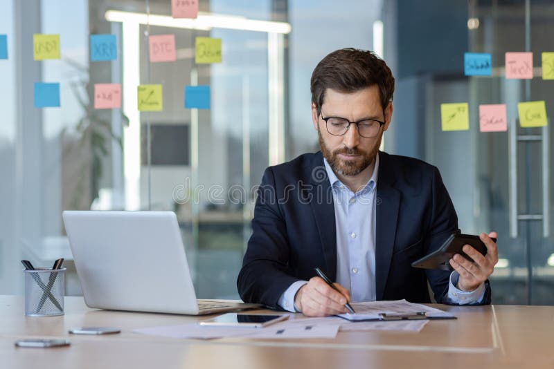Serious Thinking Businessman Using Calculator and Writing Notes in ...