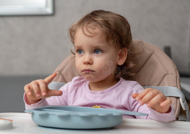 A Serious Toddler Sitting at the Table, Observing Her Surroundings with ...