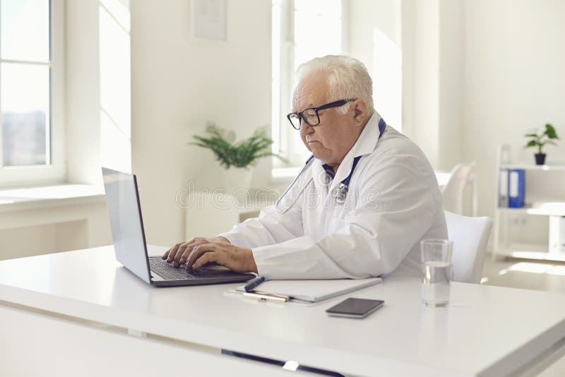 Serious White-haired General Practitioner Working on Laptop Sitting at ...