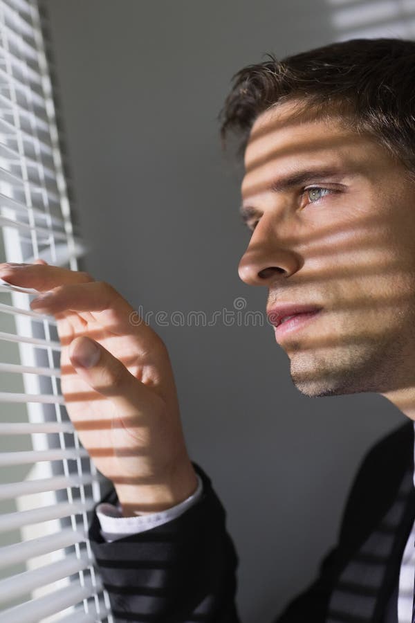 Serious Young Businessman Peeking through Blinds in Office Stock Photo ...