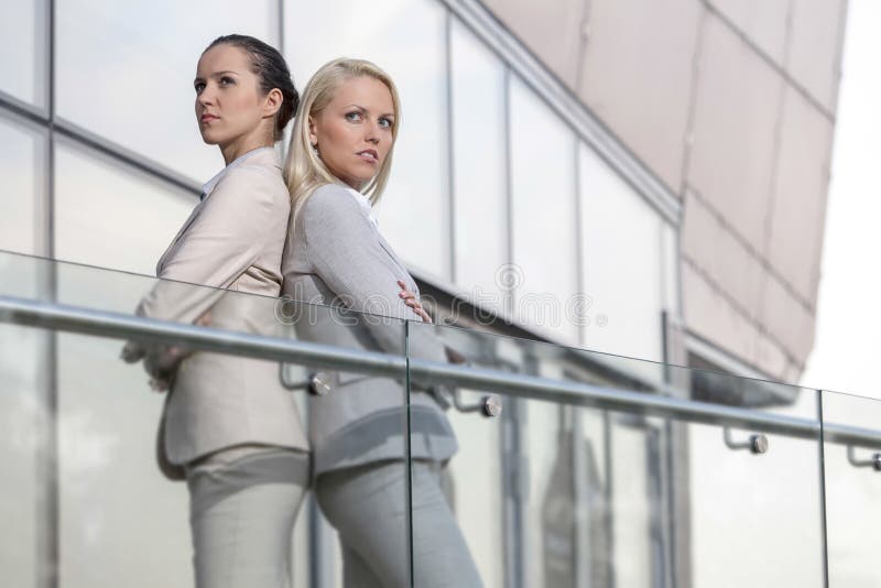 Serious Young Businesswomen Standing Back To Back at Office Railing ...