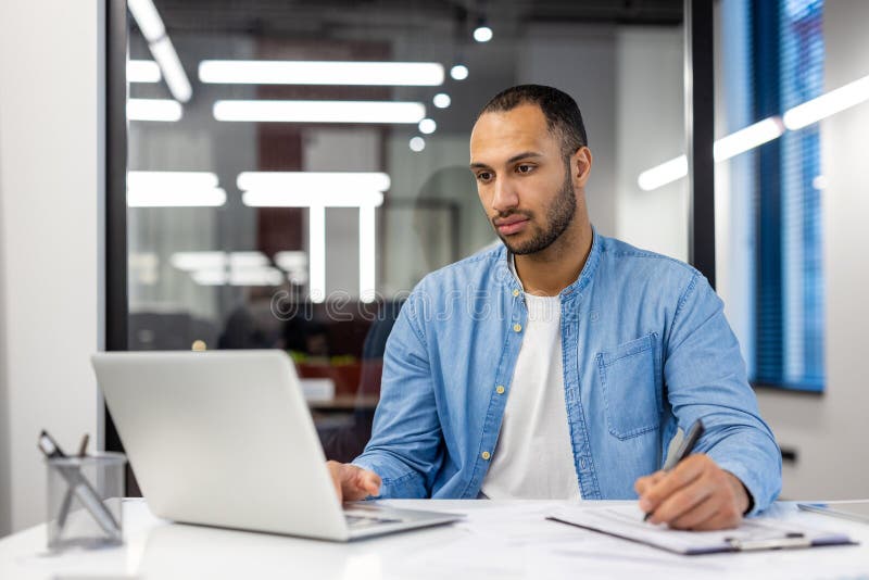 Serious Young Hispanic Man Working in Office at Desk with Laptop and ...