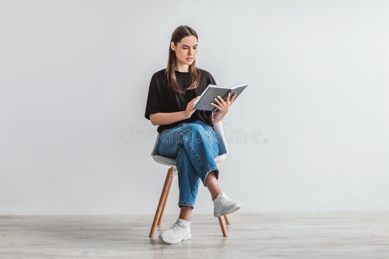 Serious Young Woman Reading Book Sitting On Chair Getting Ready For