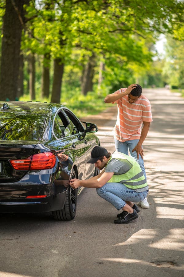 Service Man Examining the Broken Wheel of a Broken Car in the Forest ...
