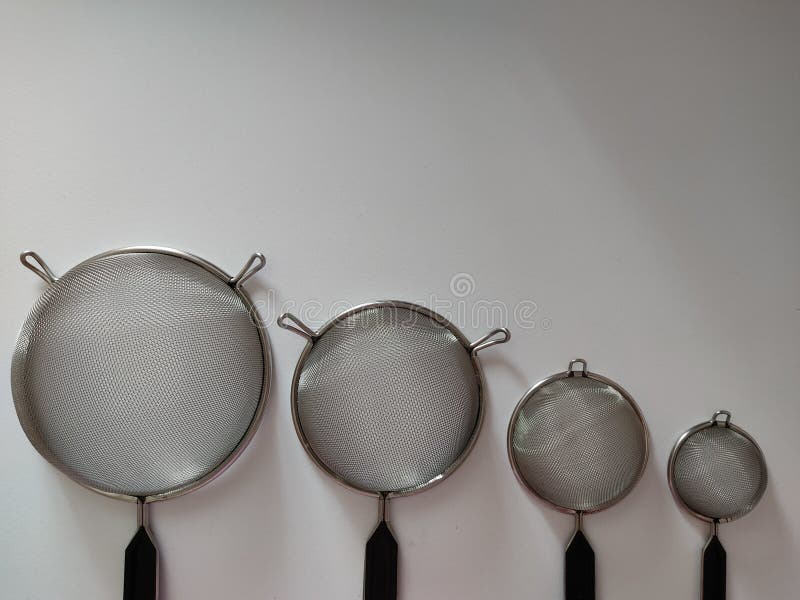 Set of Different-sized Mesh Strainers Hanging on the Gray Wall; a Copy ...