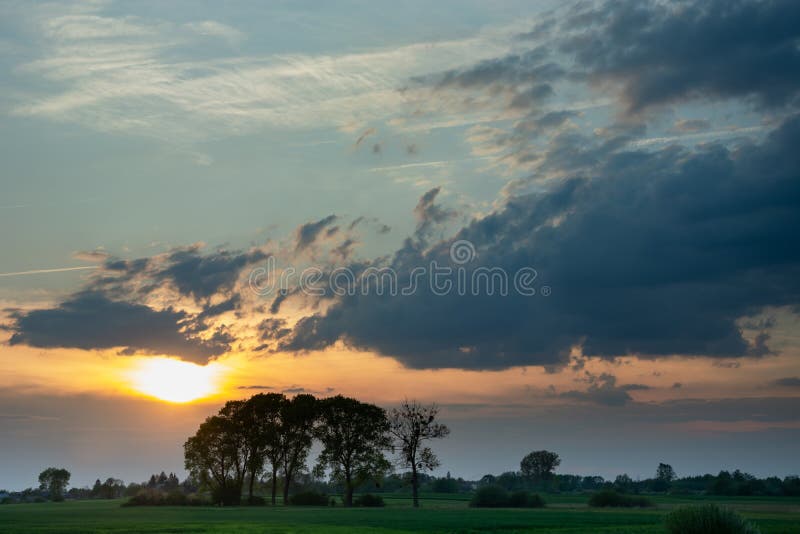 Setting Sun Behind the Clouds and Trees on the Meadow Stock Image ...