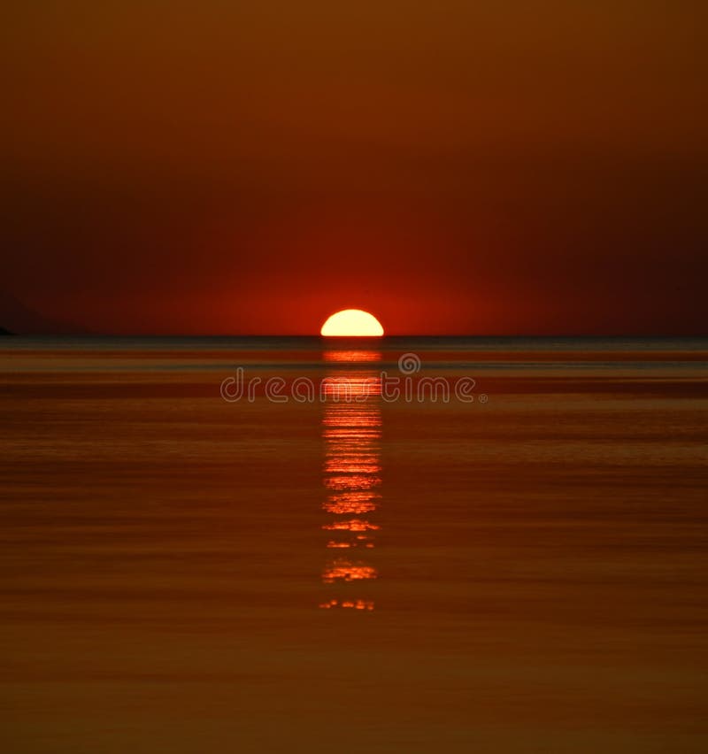 The Sun Setting on a Calm Lake with Clouds Reflected in it Stock Image ...