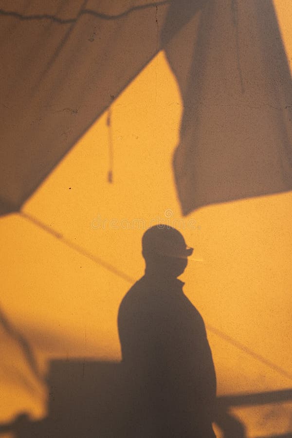 A Shadow on a Yellow Wall Cast by a Man in Glasses and a Draped Cloth ...