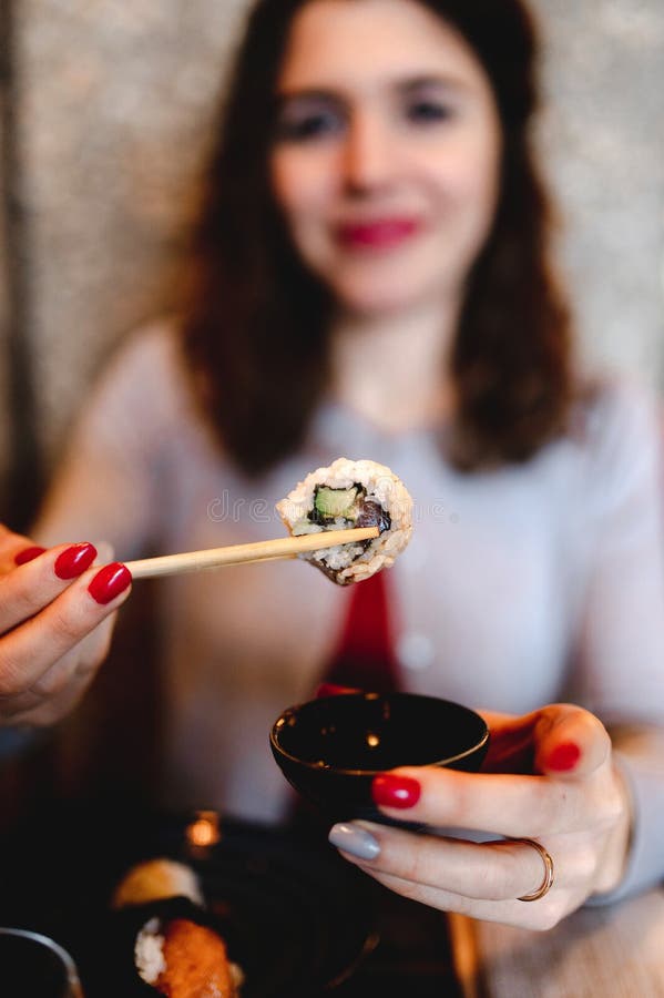 Shallow Focus of a Smiling Curly Woman Holding Sushi with Chopsticks ... Shallow Focus of a Smiling Curly Woman Holding Sushi with Chopsticks ...