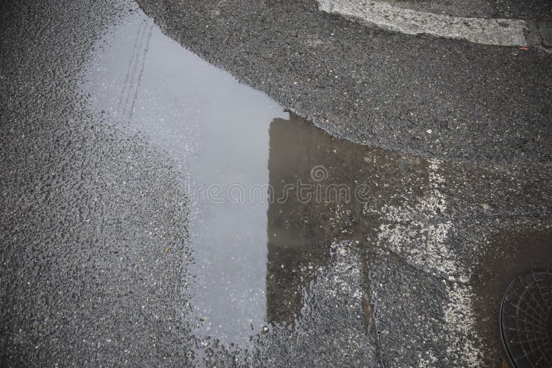 A Puddle Reflects the Surroundings on a Dark Asphalt Street. Rainwater ...