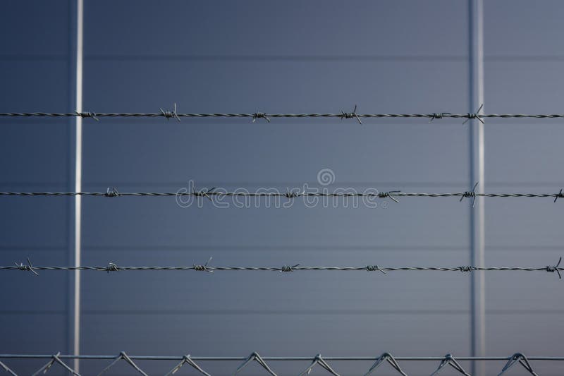 Sharp Metal Barbed Wire in Front of a Blue Warehouse.. Stock Image ...