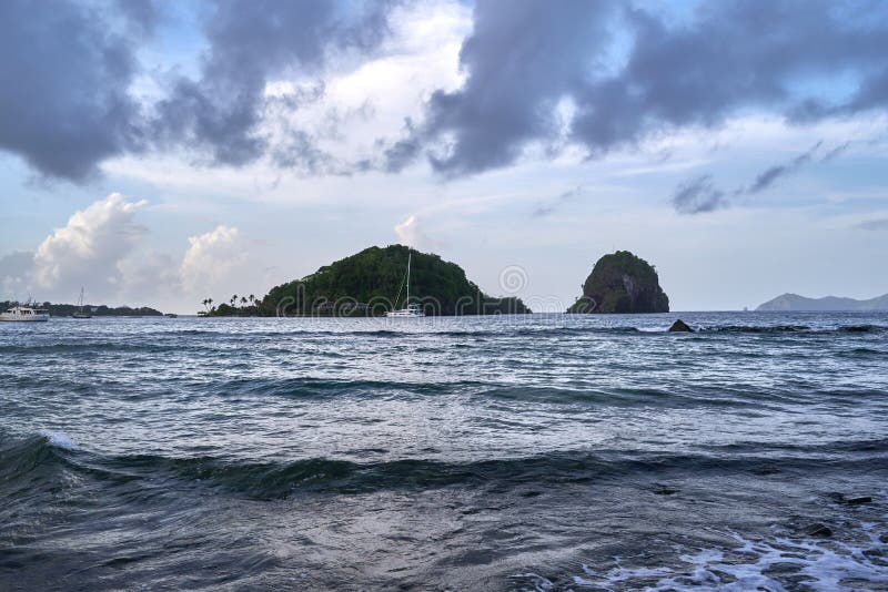 Ship in Front of Large Volcanic Rocks Covered in Trees in the Middle of ...