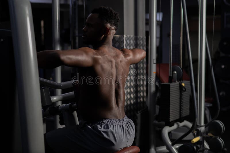 Shirtless African American Man Doing Back Exercises on a Machine in the ...