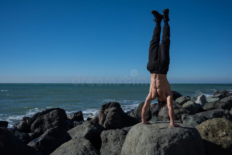 Shirtless Man Doing Handstand on Rocks by the Sea. Stock Image - Image ...