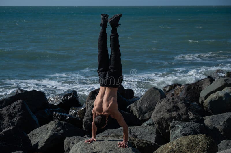 Shirtless Man Doing Handstand on Rocks by the Sea. Stock Photo - Image ...