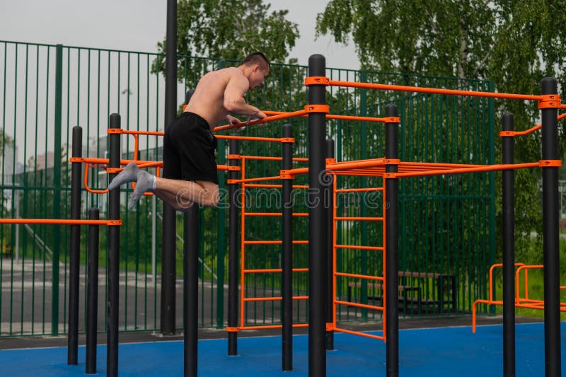 A Shirtless Man is Doing a Workout on the Horizontal Bars Outdoors ...